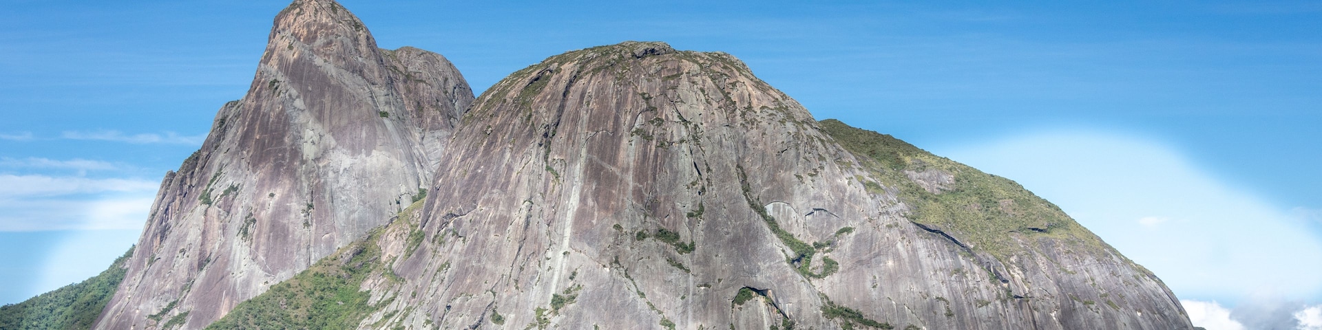 Uma montanha imponente e acidentada, com penhascos íngremes e uma densa floresta verdejante na base.