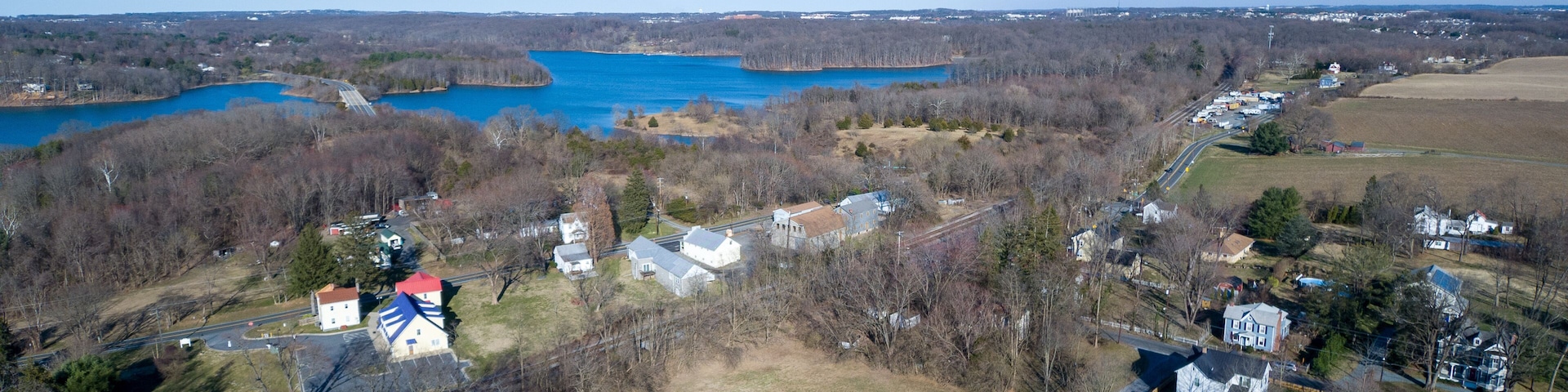 Vista aérea de uma comunidade à beira de um lago, com casas, estradas e uma barragem.