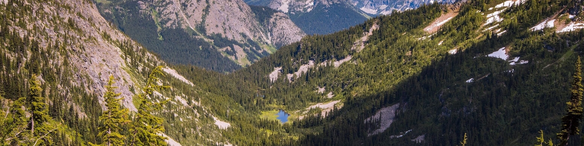 Paisagem montanhosa com um lago rodeado por florestas densas e picos rochosos.