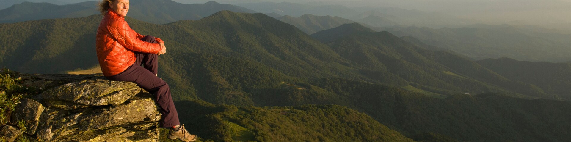 Uma pessoa sentada sobre uma rocha, com uma paisagem montanhosa ao fundo.
