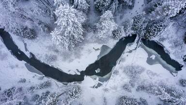 Vista aérea de uma paisagem coberta de neve, com um rio congelado e uma floresta densa.