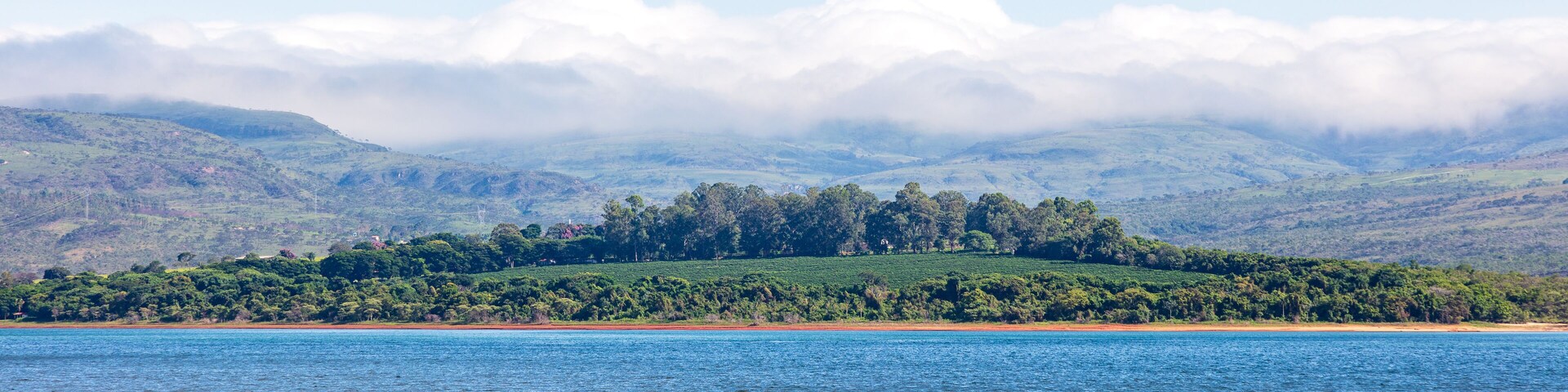 Um lago calmo com uma ilha arborizada e montanhas ao fundo.
