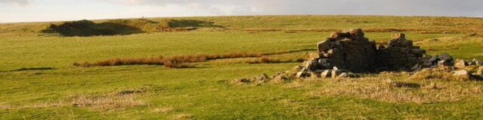 Um campo gramado com uma estrutura de pedra ao centro.