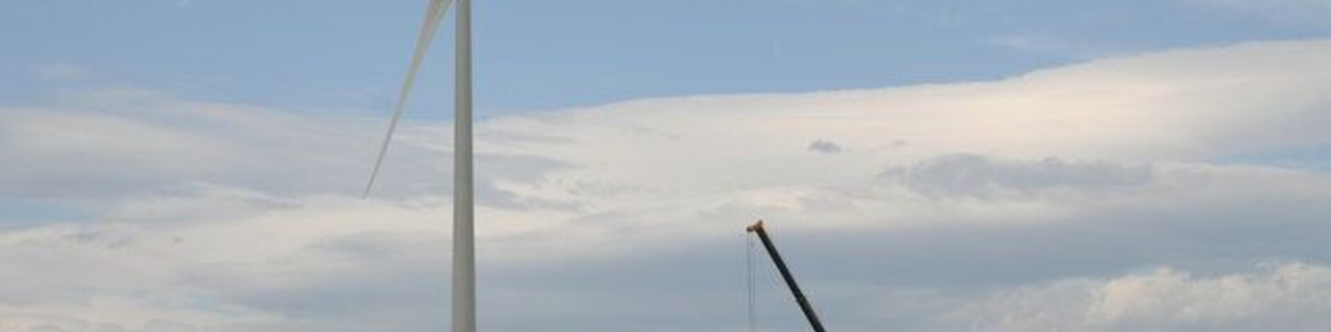 Uma turbina eólica e uma grua em um campo sob um céu nublado.