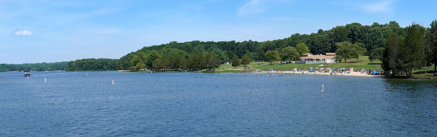 Um lago com barcos, uma praia e uma colina arborizada.