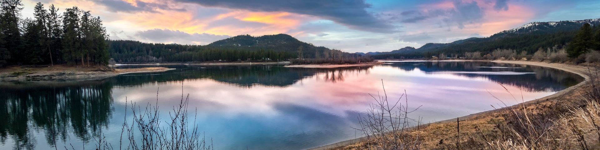 Um lago tranquilo refletindo o céu, rodeado por colinas e vegetação rasteira.