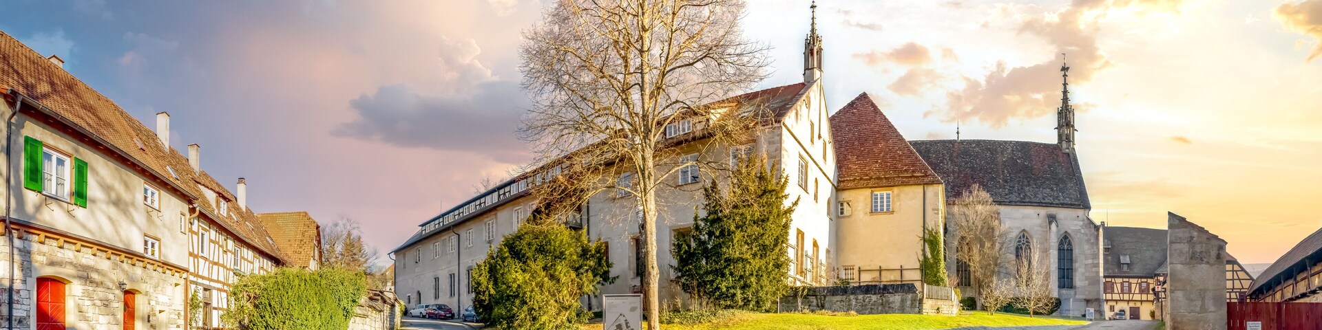 Uma rua de paralelepípedos em uma vila europeia, com edifícios históricos, uma igreja e céu claro.