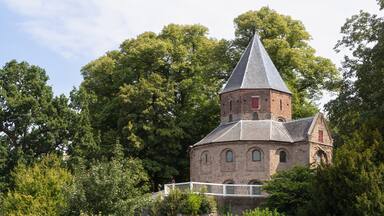 Uma igreja histórica com uma torre alta cercada por vegetação exuberante.