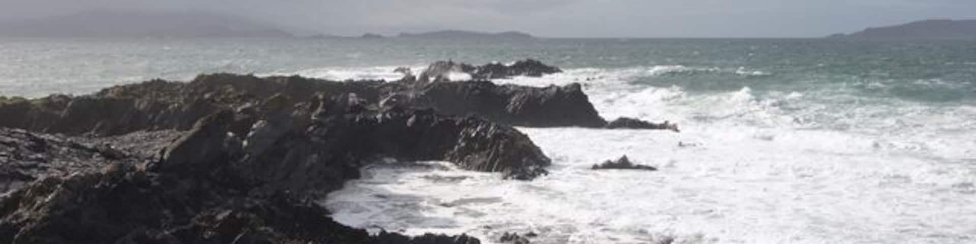 Uma costa rochosa com ondas quebrando nas pedras sob um céu nublado.