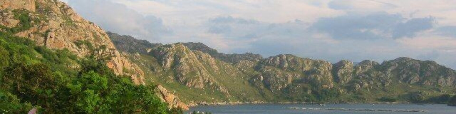 Paisagem costeira com montanhas, uma praia e um pequeno povoado.