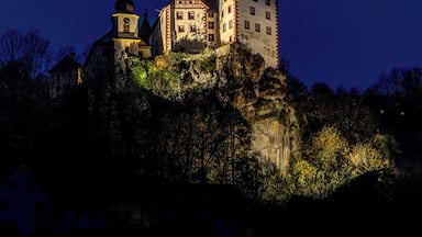 Um castelo imponente sobre um penhasco, com janelas iluminadas e uma torre do relógio.