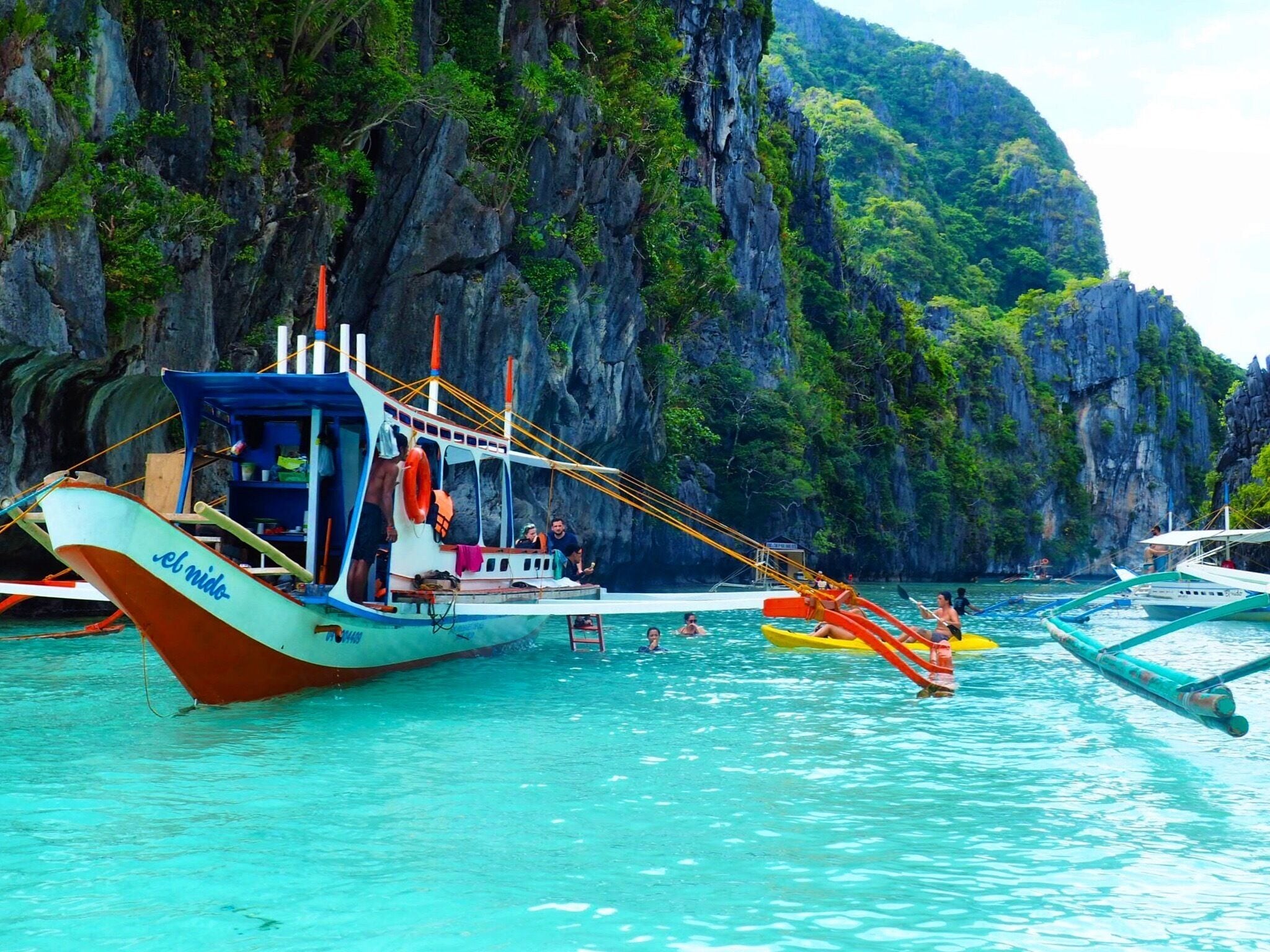 Um barco chamado 'el nido' atracado perto de um penhasco rochoso com águas turquesa cristalinas.