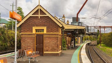 Uma estação de trem de tijolos com uma porta marrom, um banco e uma plataforma com um caminho de piso tátil verde.