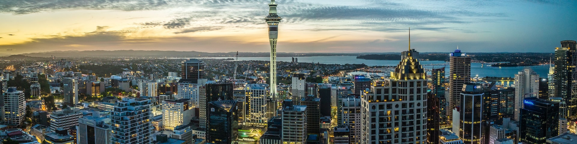 Paisagem urbana com uma torre imponente, edifícios urbanos densos e um corpo d'água ao longe.
