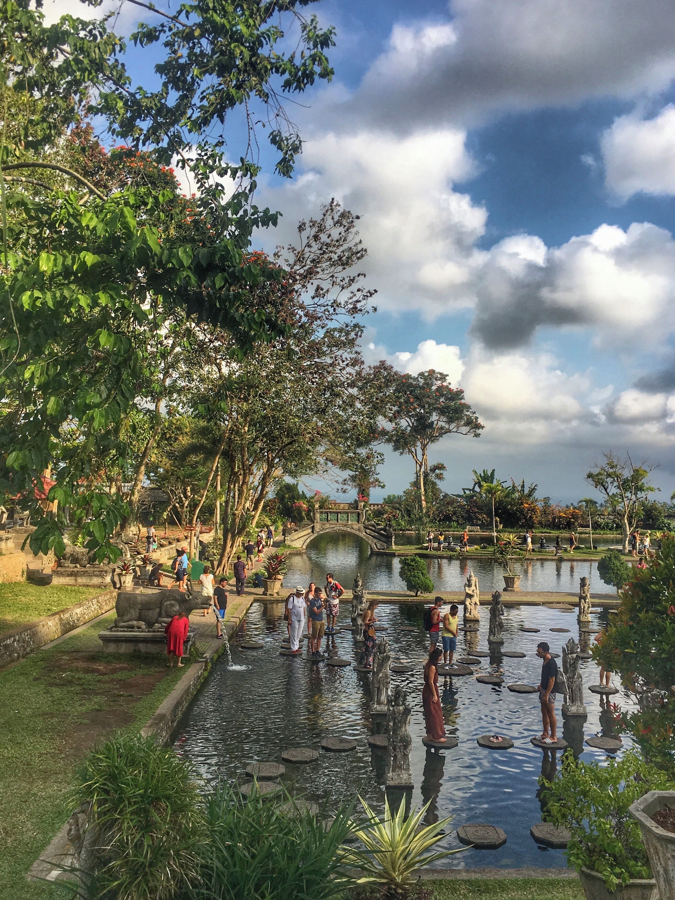 Um parque com lago, pessoas caminhando e uma ponte.