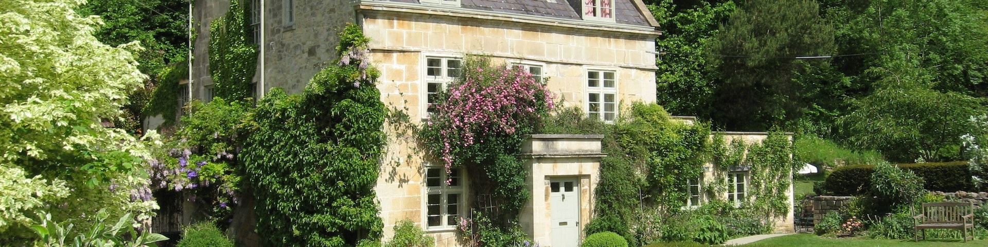 Uma casa de pedra com jardim, rodeada por árvores.