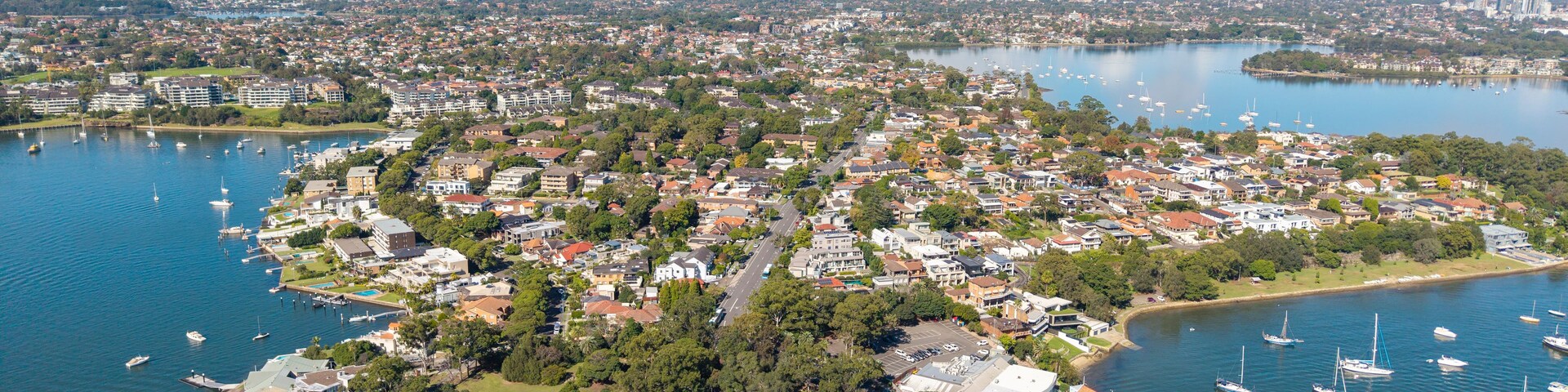 Vista aérea de uma cidade costeira com um porto de iates, áreas residenciais e uma grande extensão de água.