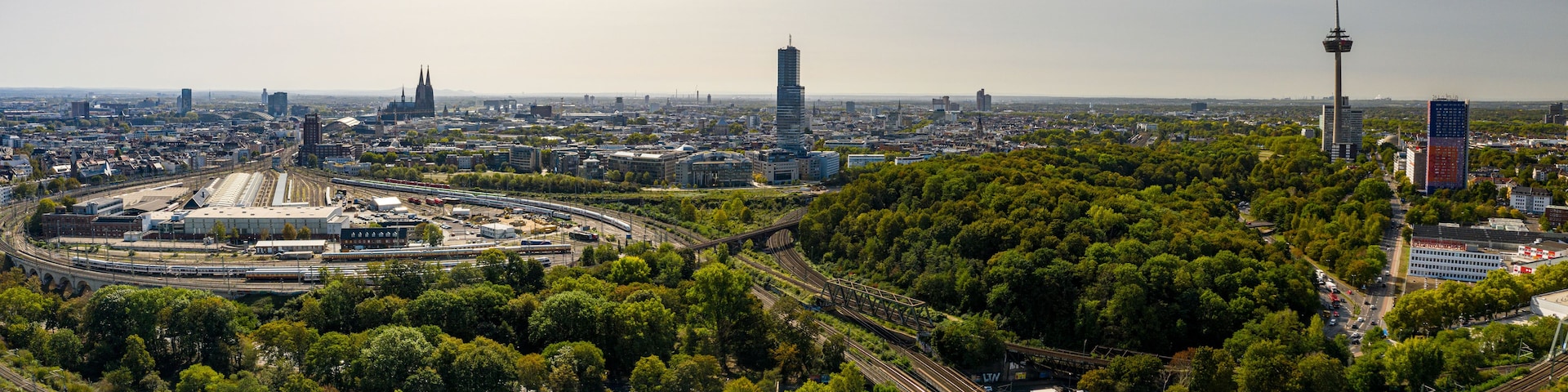 Paisagem urbana com uma torre imponente, vegetação densa e uma extensa rede ferroviária.