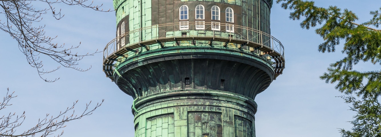 Uma torre verde com topo arredondado e uma agulha, rodeada por árvores.