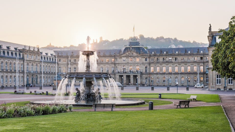 Um edifício histórico imponente com uma fonte central e jardins bem cuidados.