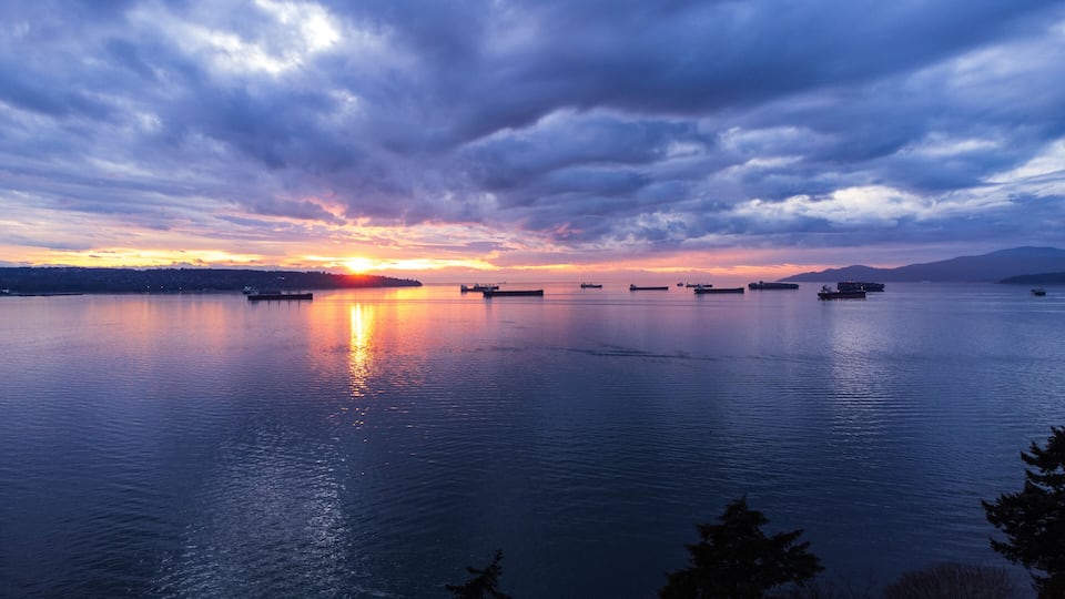 Um pôr do sol sobre um lago tranquilo com vários barcos, uma linha de costa distante e uma cordilheira.