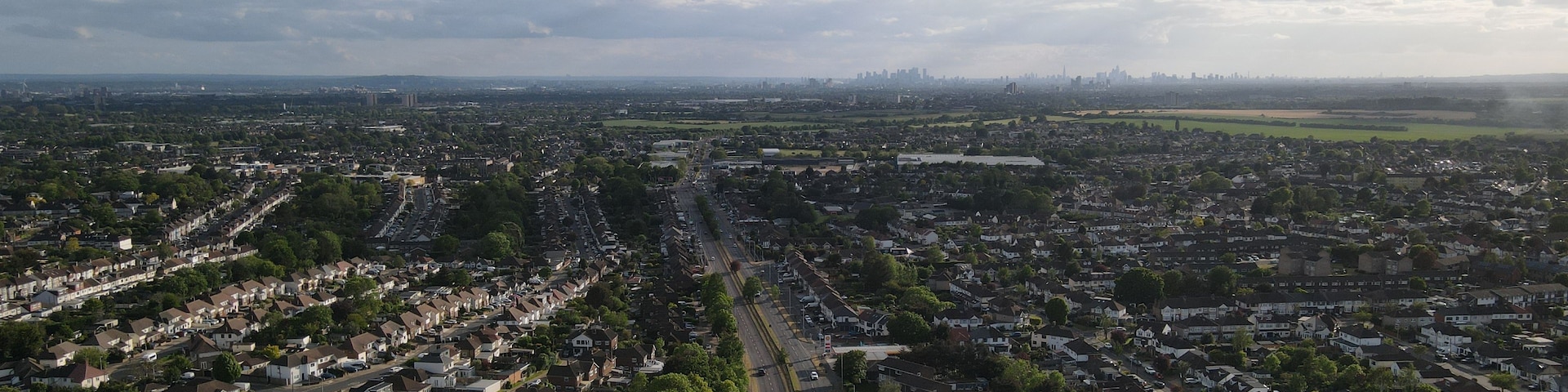 Vista aérea de um bairro residencial com casas, ruas e o horizonte de uma cidade ao longe.