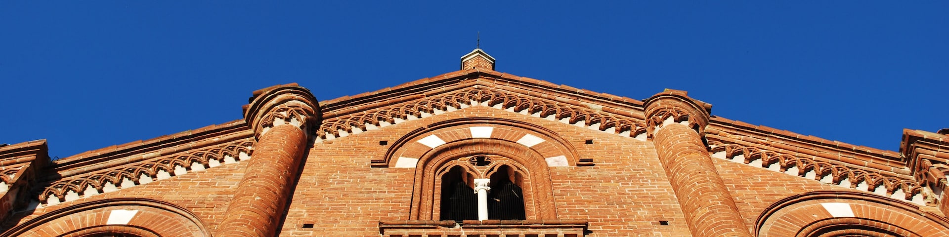 Um edifício grande de tijolos com uma entrada em arco notável e um céu azul claro acima.