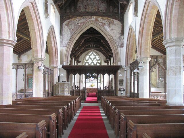 Interior de uma igreja com bancos de madeira, um tapete vermelho e arcos góticos.