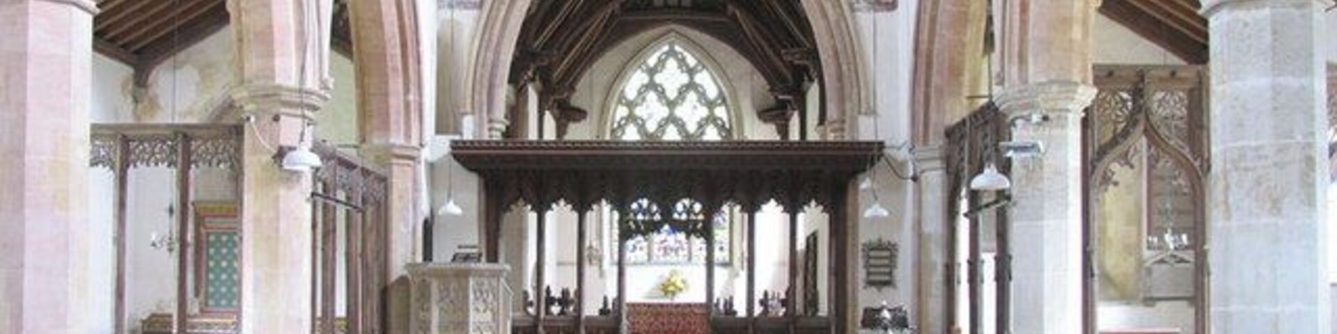 Interior de uma igreja com bancos de madeira, um tapete vermelho e arcos góticos.