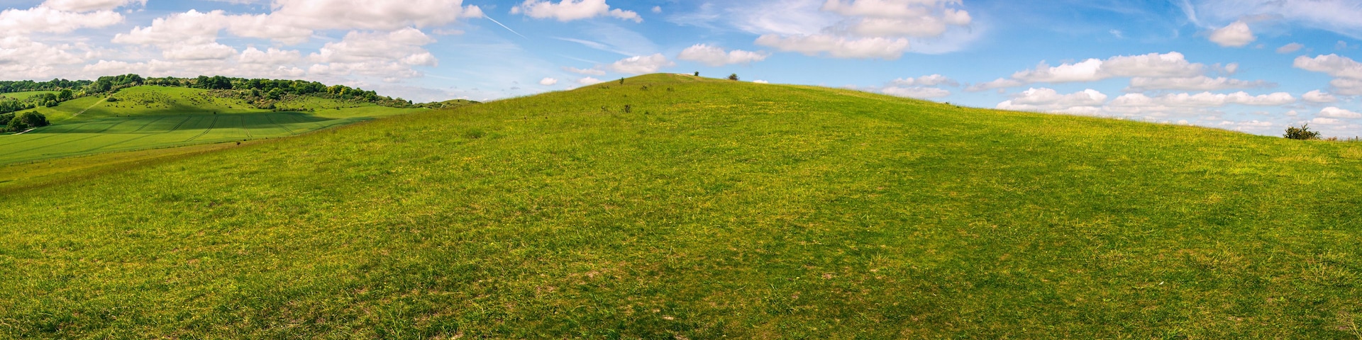 Uma colina verde com céu claro e algumas nuvens.