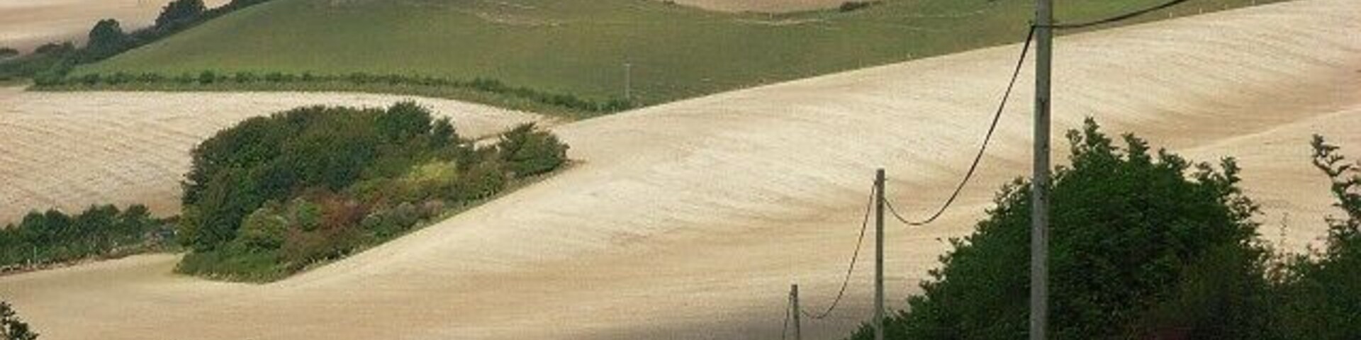 Paisagem rural com colinas ondulantes, estrada sinuosa e campos.