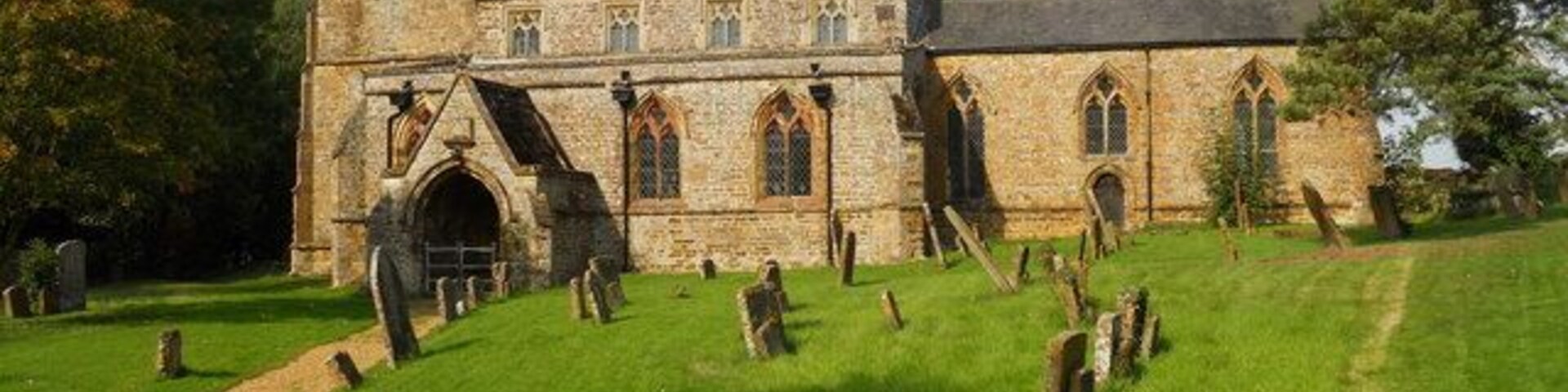 Uma igreja histórica com uma torre imponente e janelas em arco, cercada por um cemitério.
