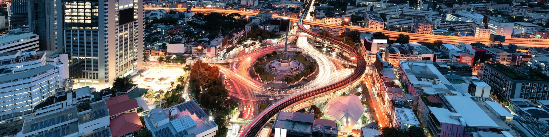 Paisagem urbana ao entardecer, com uma rotatória em destaque e edifícios altos ao redor.