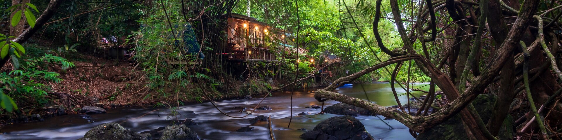 Um rio serpenteando por uma floresta, com uma estrutura de madeira na margem direita.