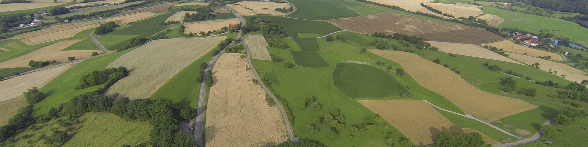Vista aérea de uma paisagem rural com campos, estradas e edifícios dispersos.