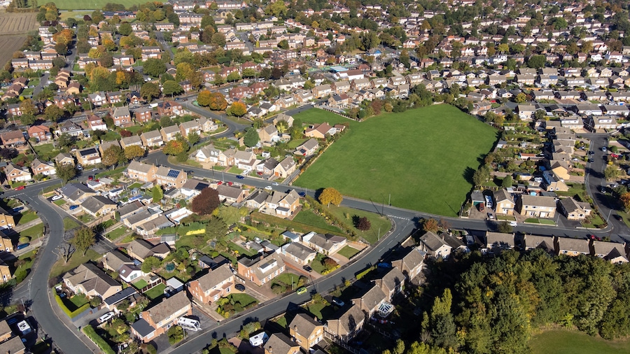 Vista aérea de um bairro residencial com casas, ruas e um grande campo verde.