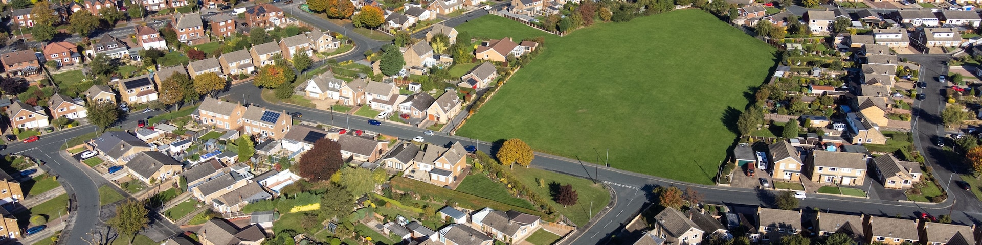 Vista aérea de um bairro residencial com casas, ruas e um grande campo verde.