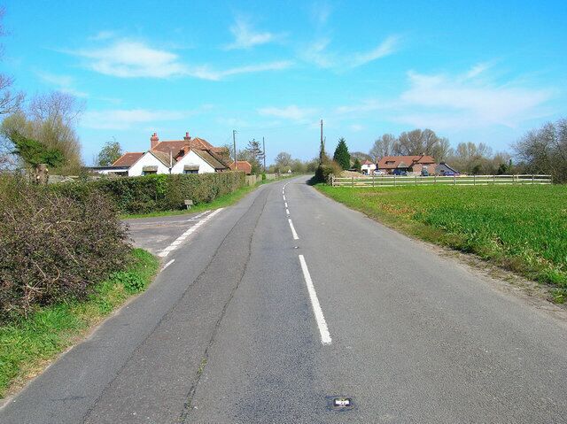 Uma estrada rural com casas de um lado e campos do outro.