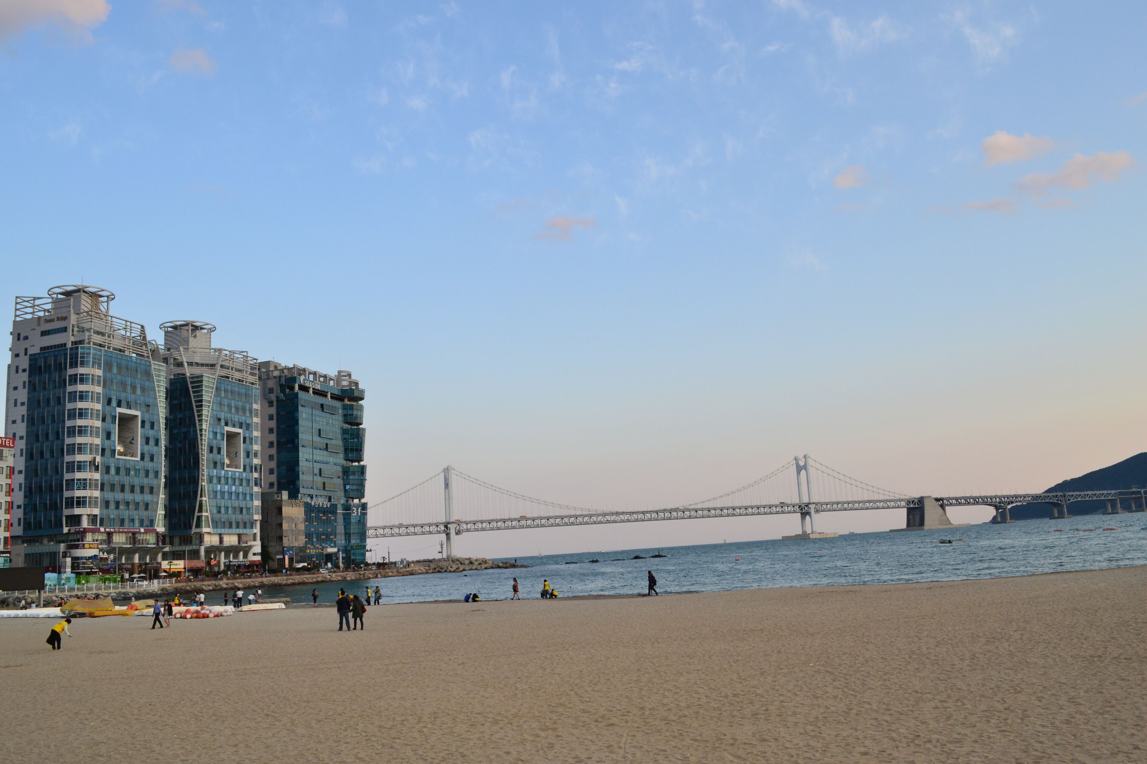 Uma praia com uma ponte grande ao fundo e edifícios modernos.