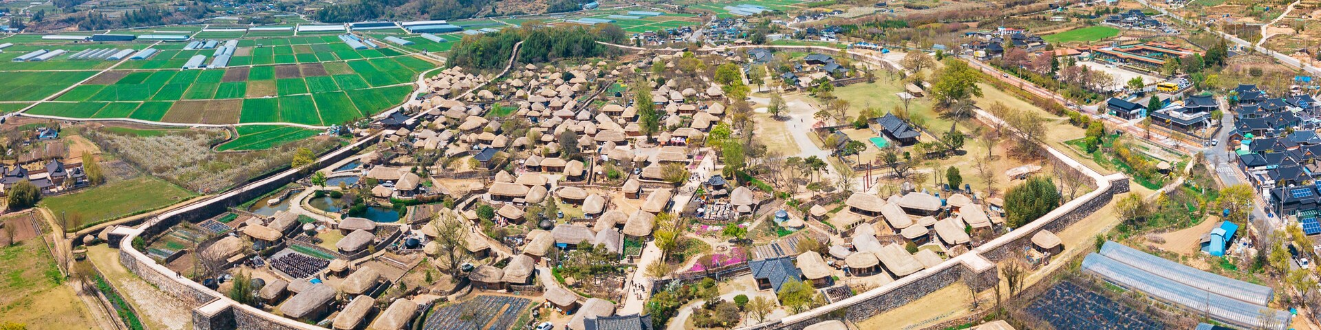 Vista aérea de uma aldeia com casas tradicionais, rodeada por campos e montanhas.