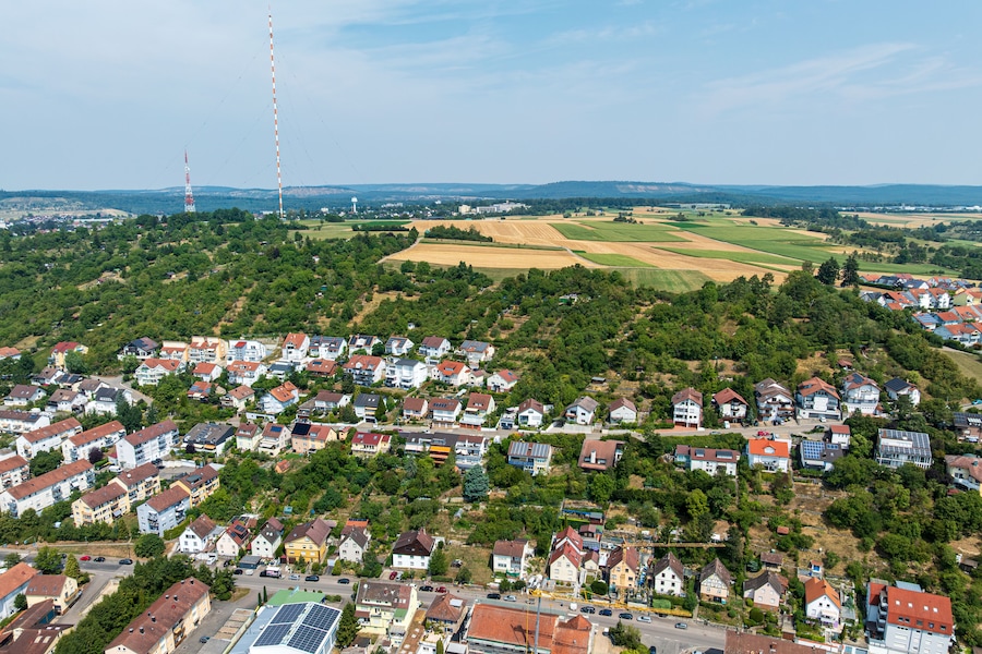 Zona residencial com casas, um campo extenso e uma turbina eólica ao fundo.