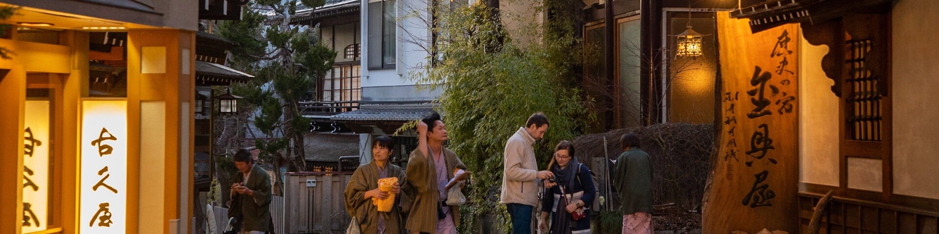 Uma rua tradicional japonesa com pedestres, edifícios de madeira e letreiros iluminados.