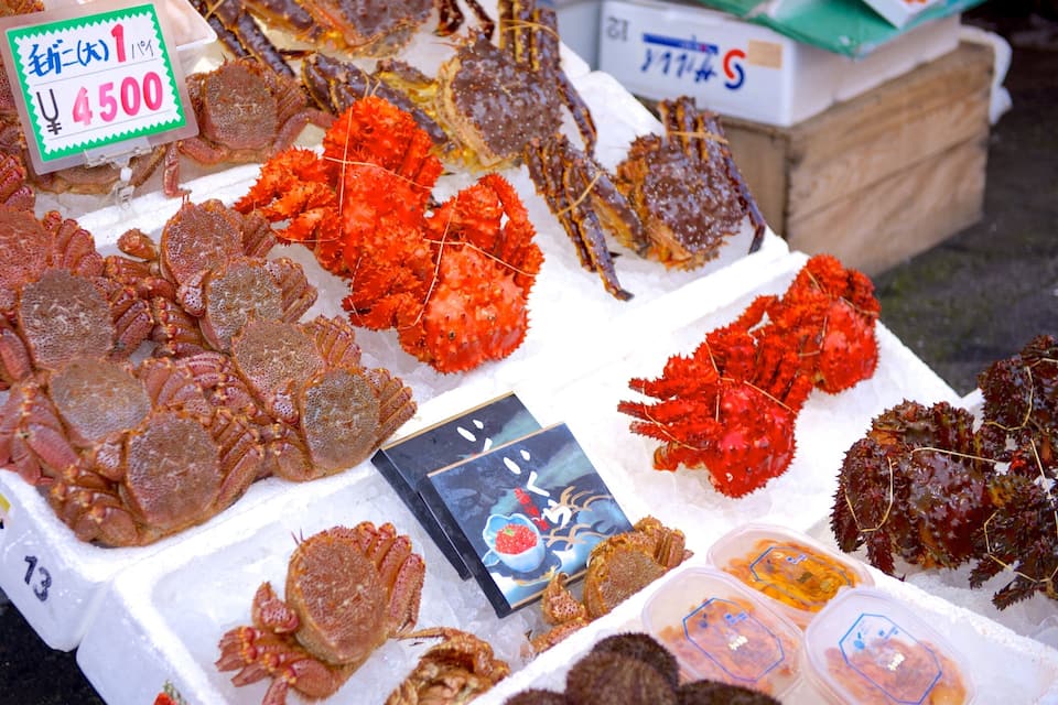 Variedade de frutos do mar, incluindo patas de caranguejo vermelho e marrom, expostas em uma bancada com gelo.