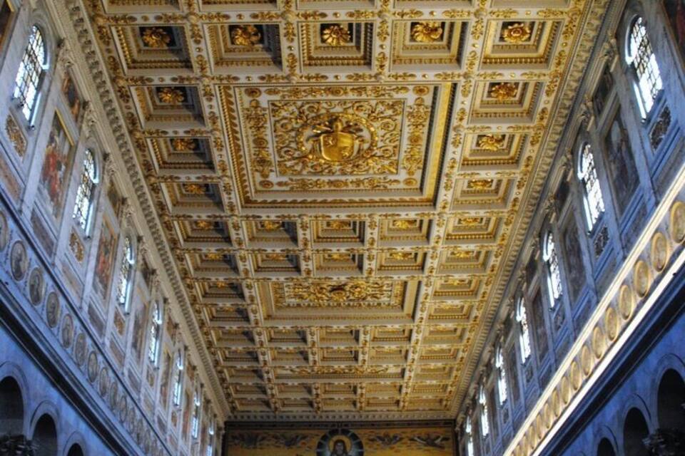 Um salão imponente com teto ricamente decorado, apresentando detalhes dourados complexos e um afresco central.