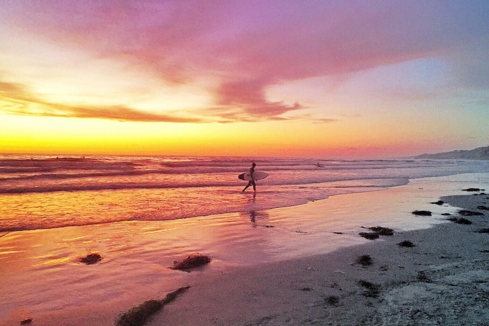 Uma praia ao pôr do sol com ondas e pegadas na areia.