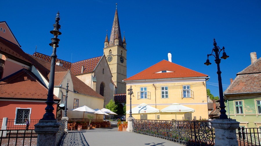Uma praça histórica com uma igreja, um edifício amarelo e mesas ao ar livre.