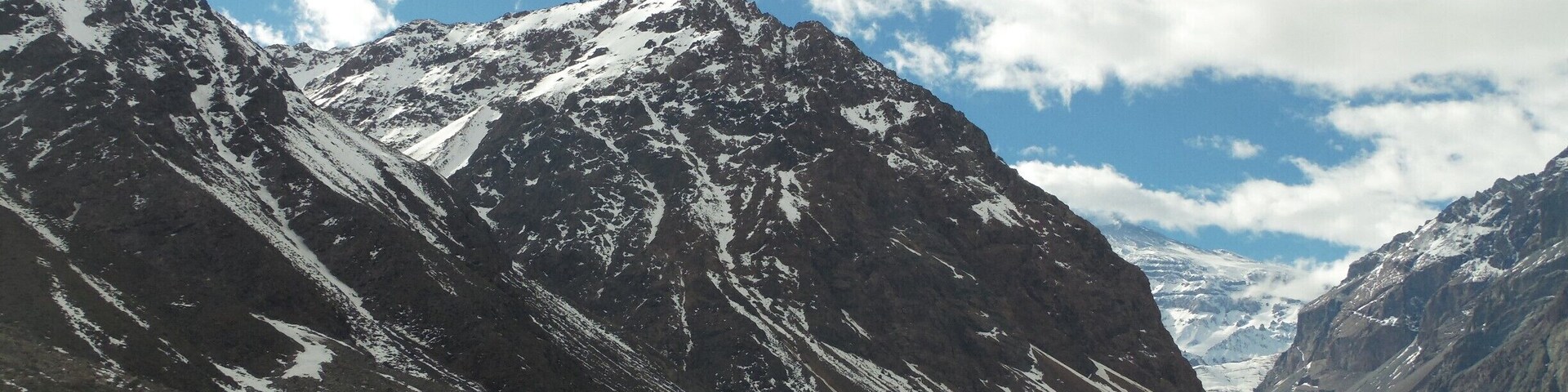 Uma cordilheira com picos nevados e um vale com vegetação densa.