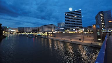 Paisagem urbana ao anoitecer com um rio, uma ponte e edifícios, incluindo SAAR-CENTER e KARLSBERG URPILS.