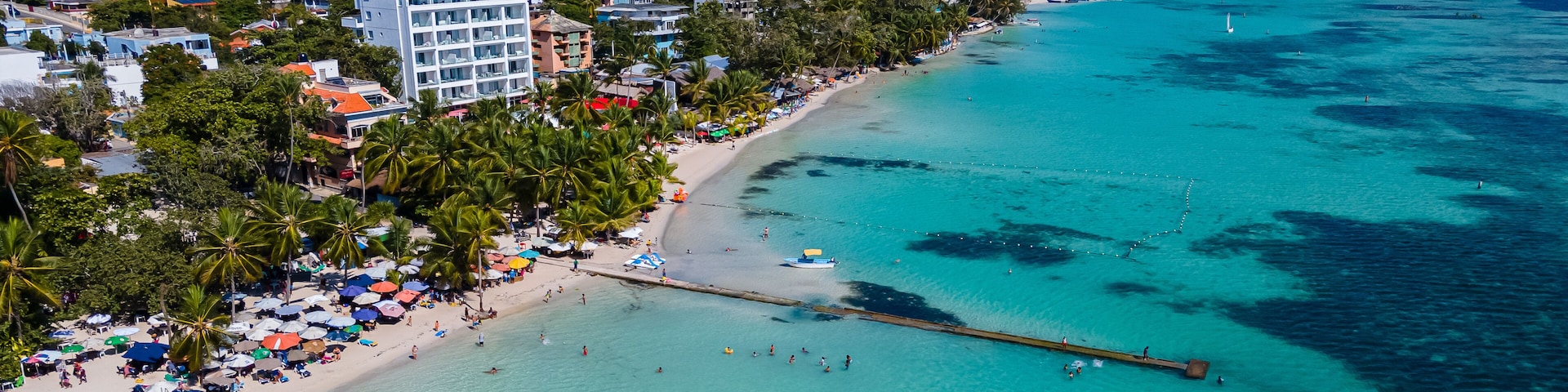 Paisagem costeira com praia, águas azul-turquesa e palmeiras.