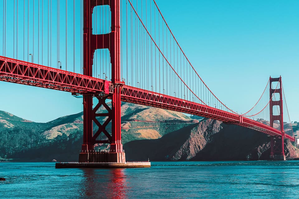 A Ponte Golden Gate estendendo-se sobre a água, com duas rochas grandes em primeiro plano e uma paisagem montanhosa ao fundo.